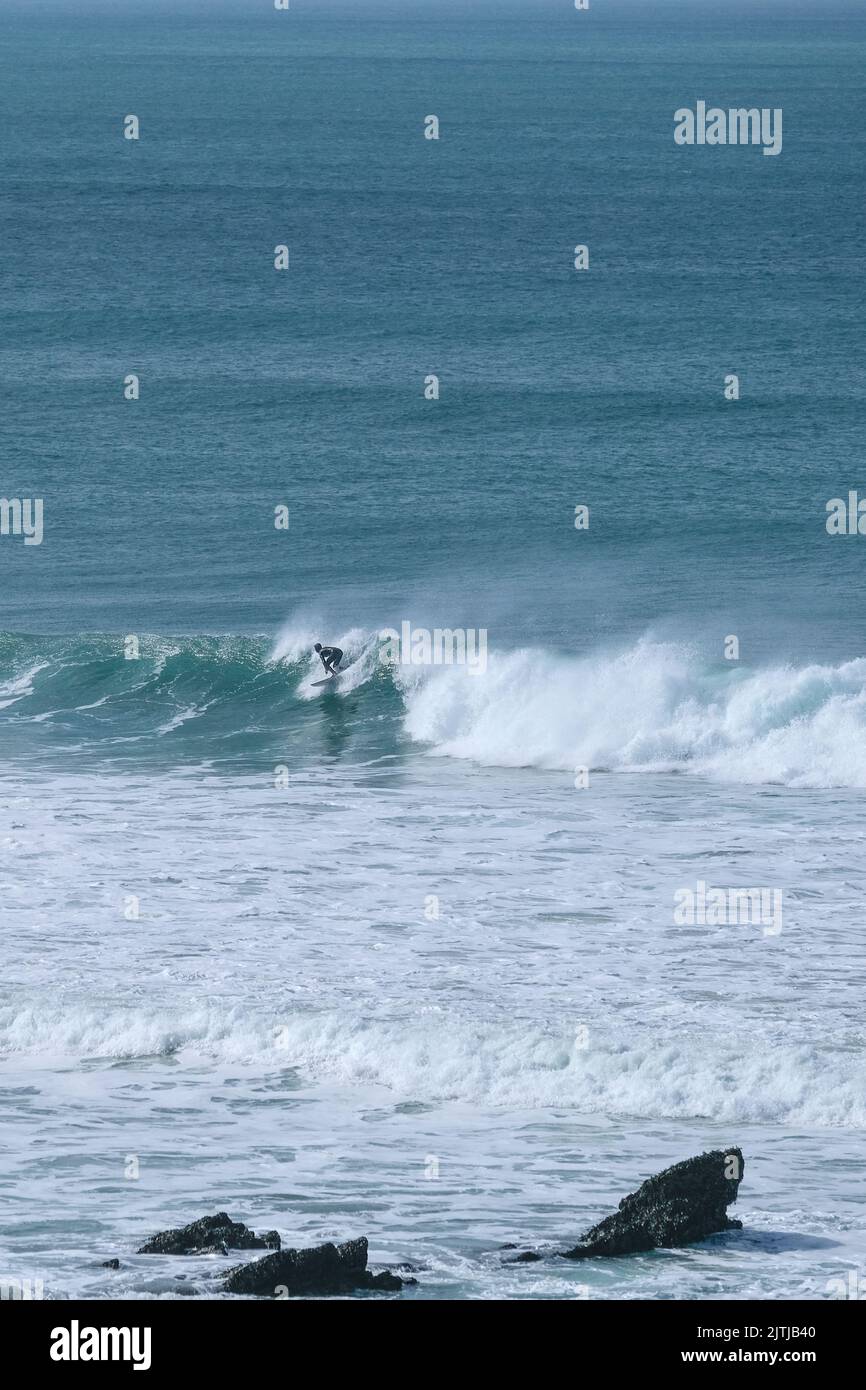 A lone surfer riding a wave in Fistral Bay in Newquay in Cornwall in ...