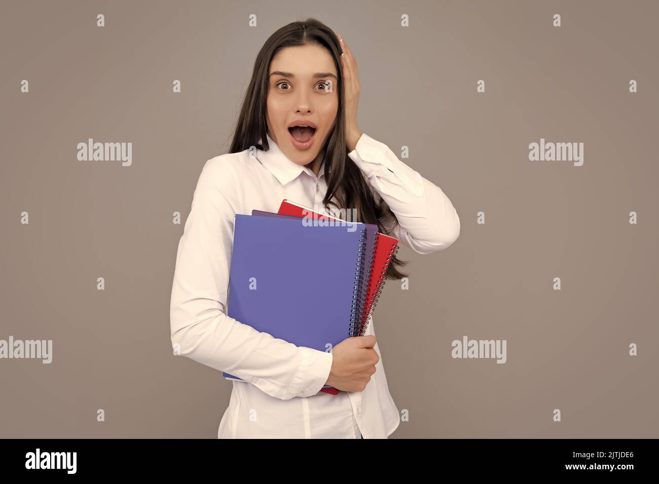Teen girl with notebooks standing over gray background with copy space ...