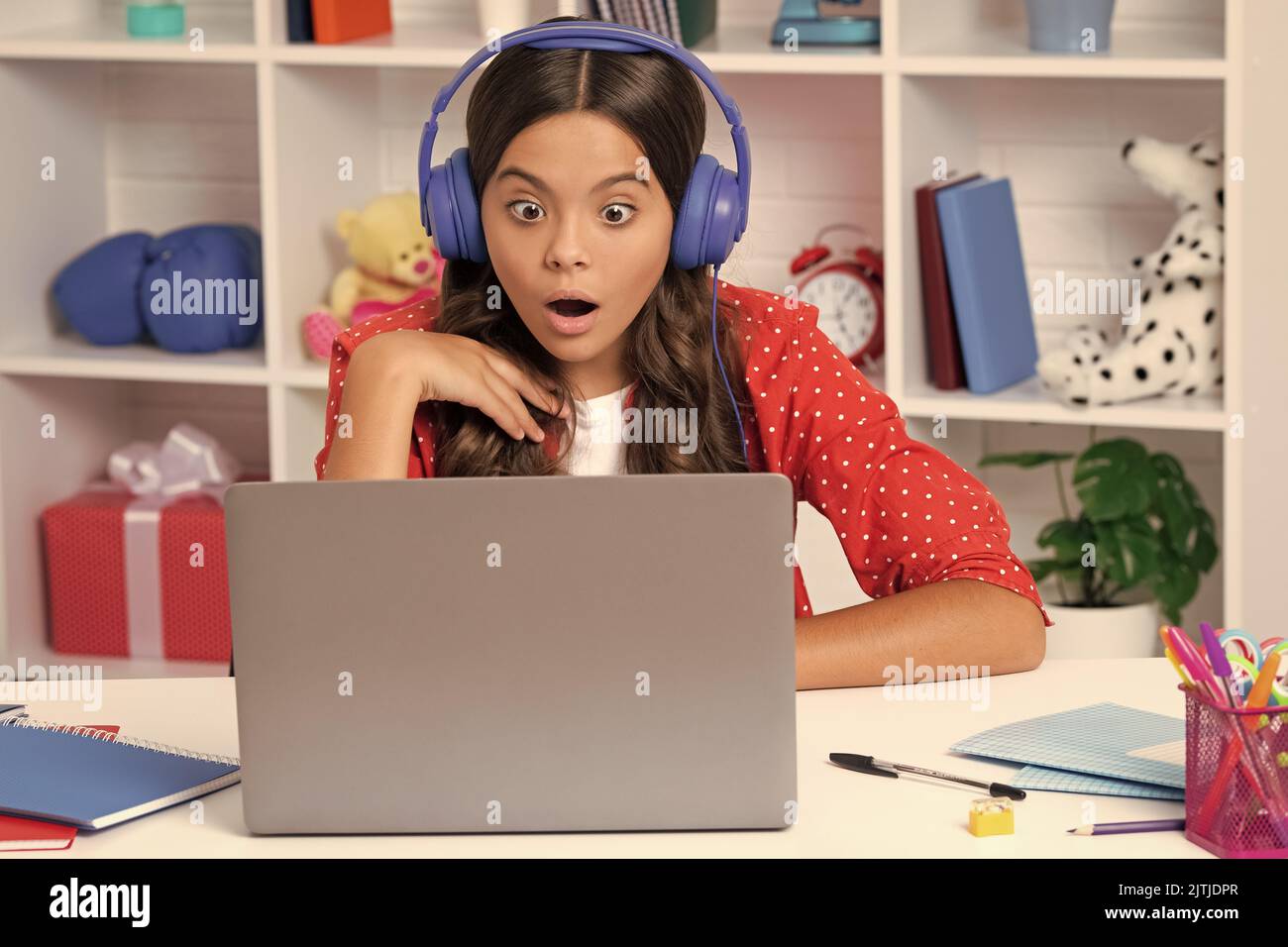 A young female student sitting at the table, using headphones and ...