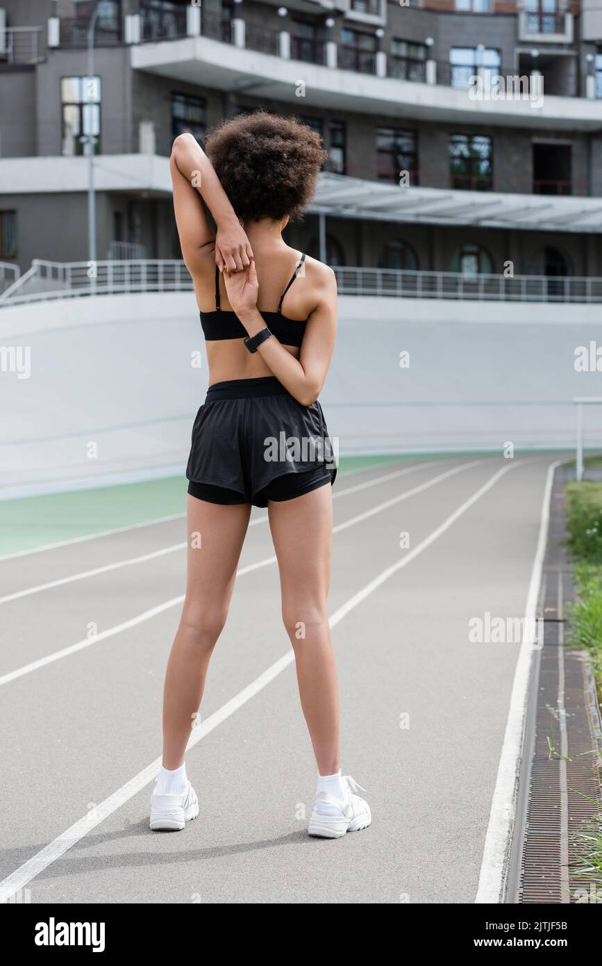 Back view of african american sportswoman stretching arms on blurred ...