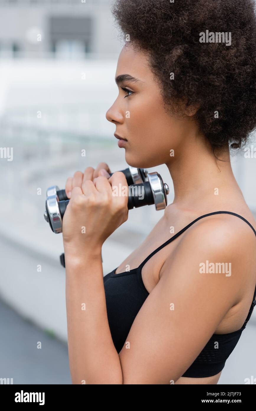 Side view of african american sportswoman training with dumbbells ...