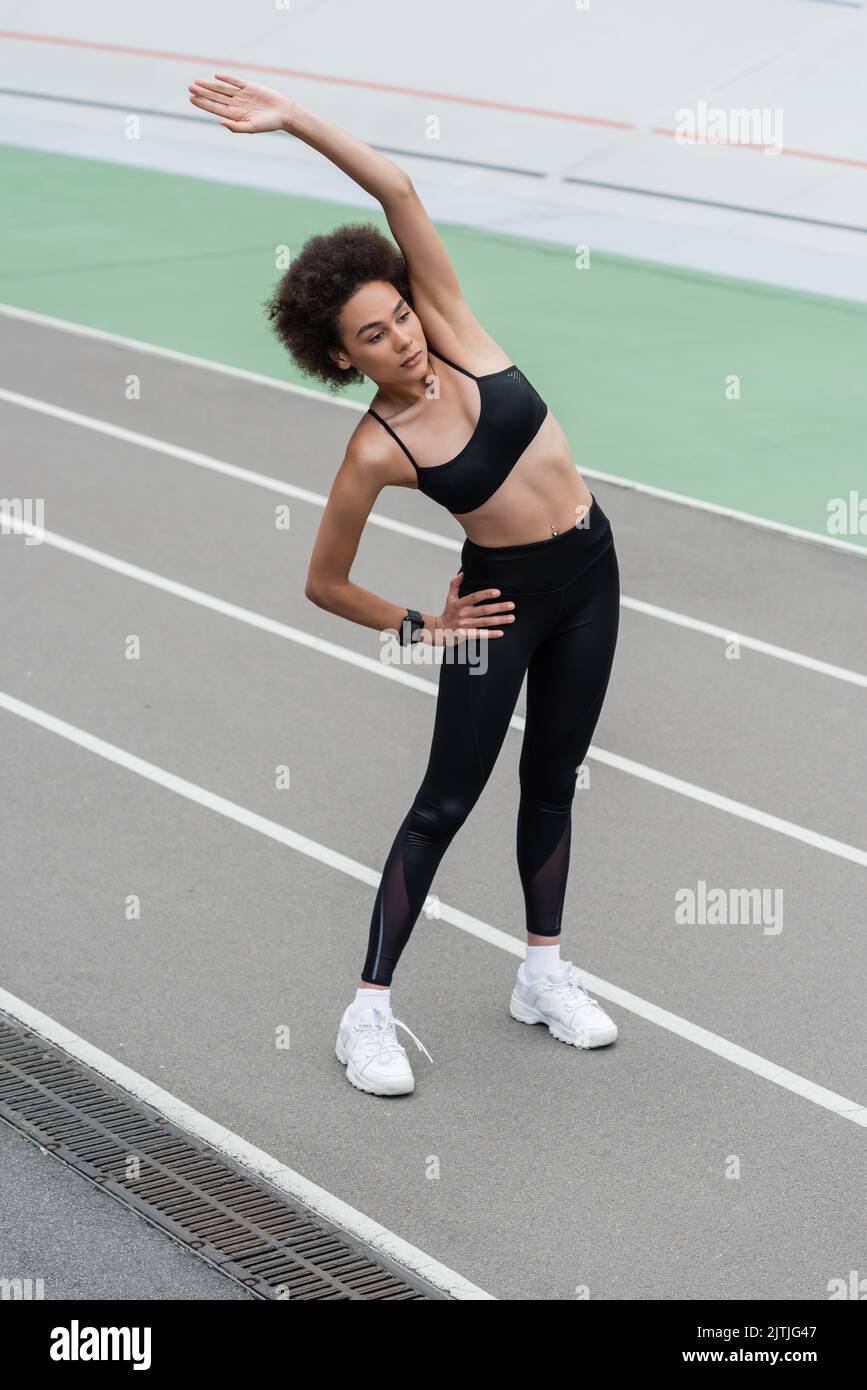 athletic african american woman in black sportswear doing side bend ...
