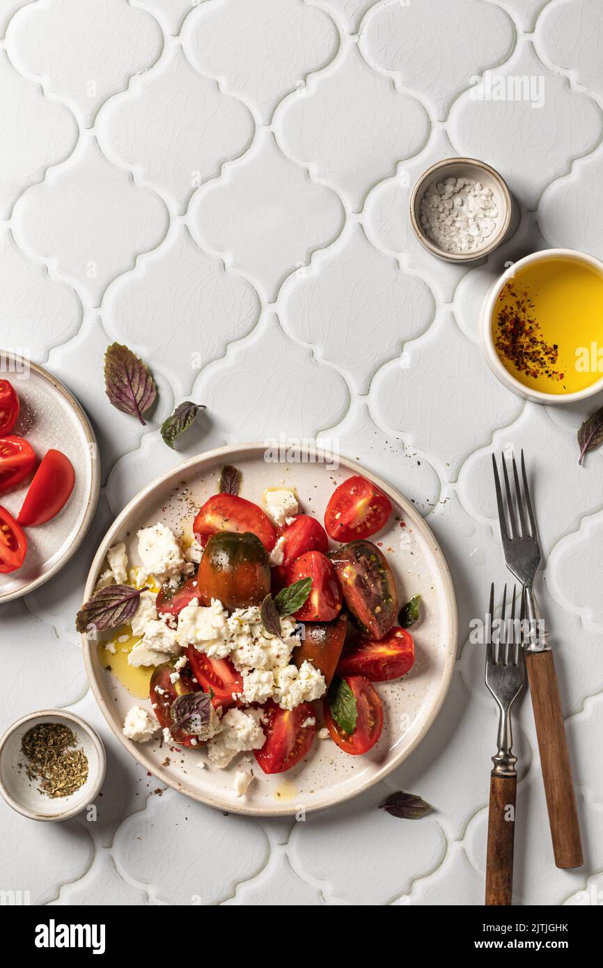 Tomato salad with feta cheese and bazil leaves served with cutlery on ...