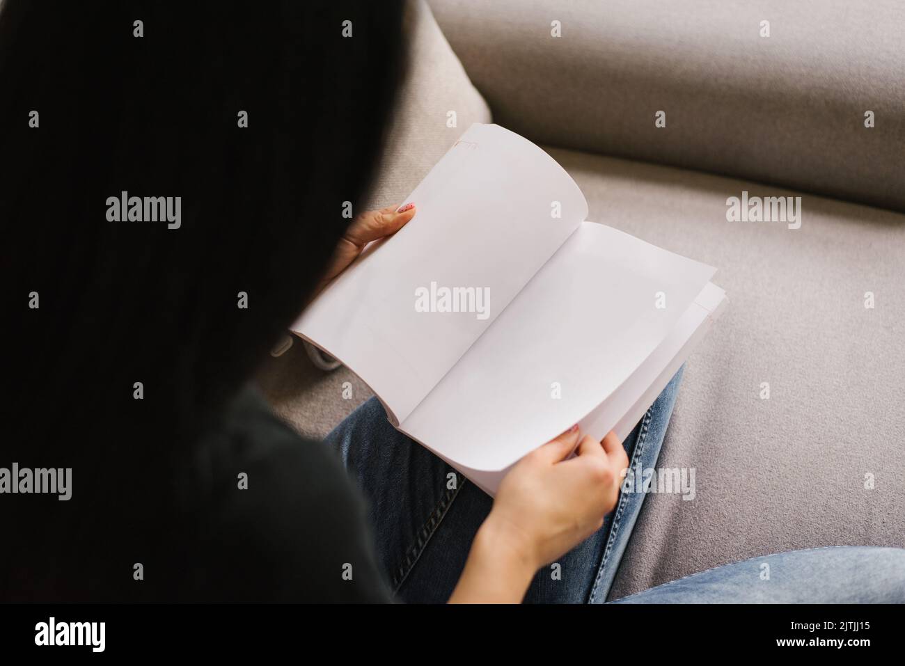 Woman is reading a book, a mockup of a blank page. View from behind the ...