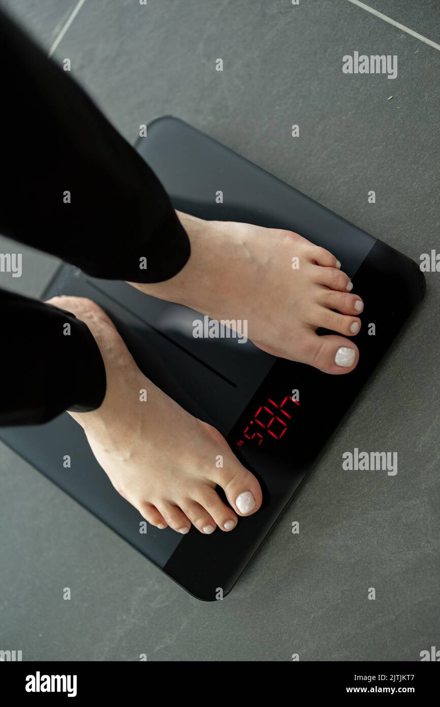 Woman measures her weight on floor scales. Female feet are on scales against the background of ...