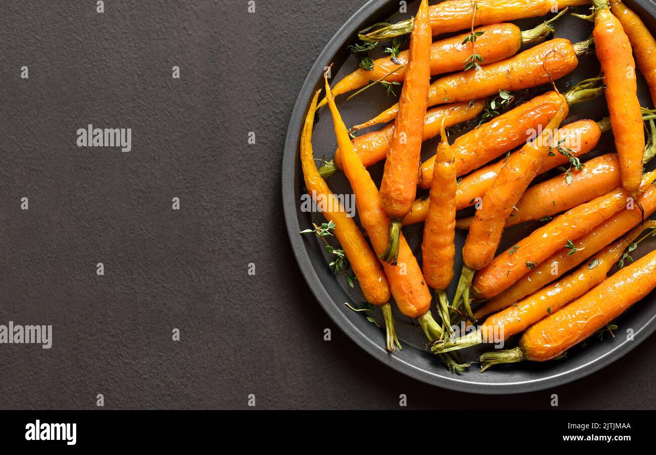 Close up view of roasted honey glazed carrots on plate over dark stone ...