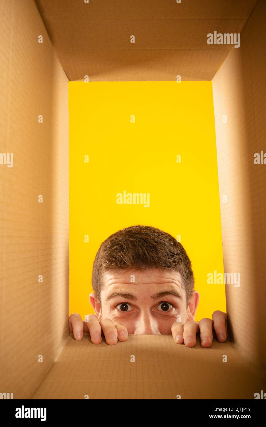 Pry into box. Charming man unpacking, opening carton box and looking ...