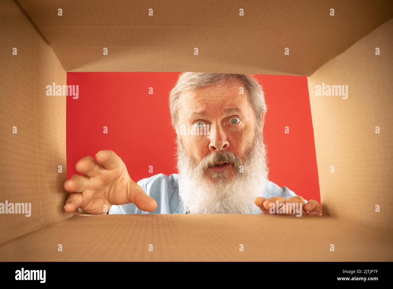 Wonder. Senior bearded man unpacking, opening carton box and looking ...