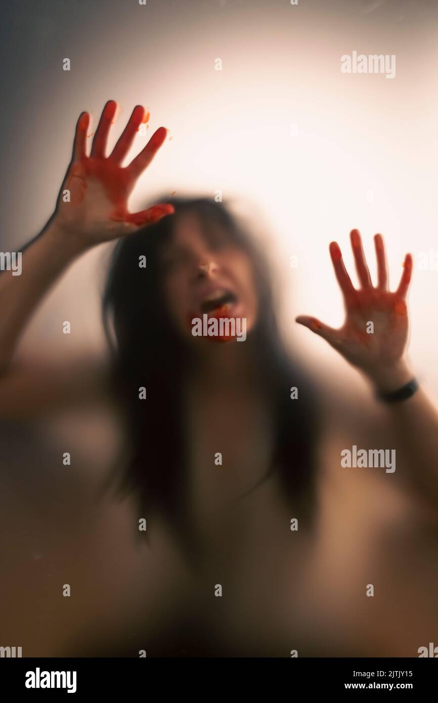 Horror ghost woman with blooded hands behind the matte glass. Halloween ...
