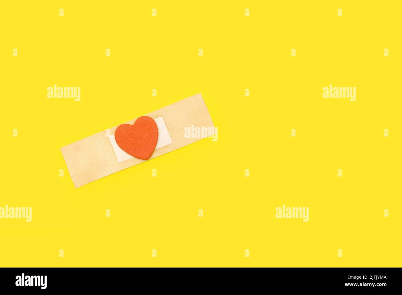 A red paper heart on an adhesive bandage on a yellow background with ...