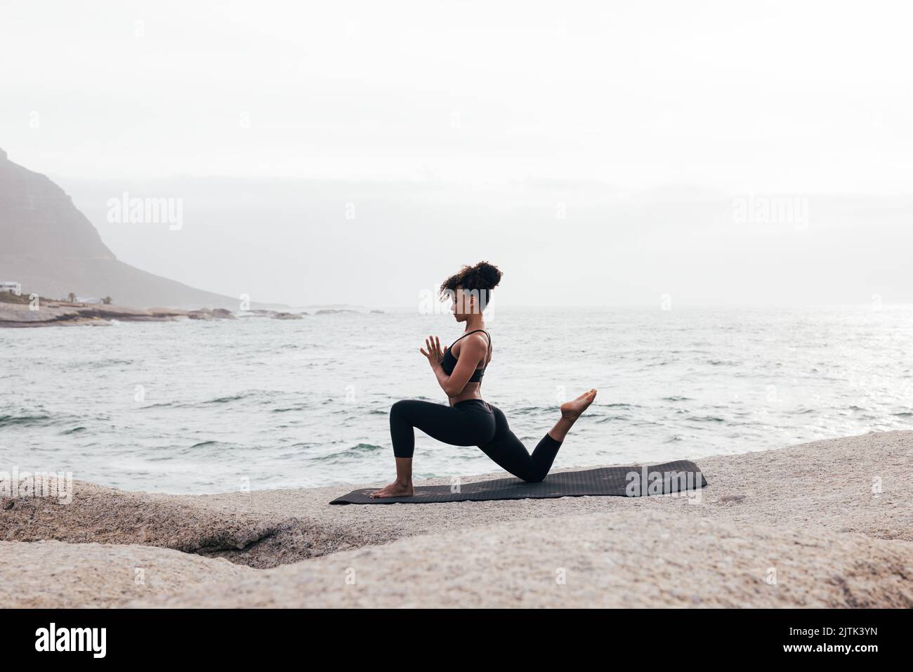 Side view of fit woman practicing yoga on mat by ocean. Female ...