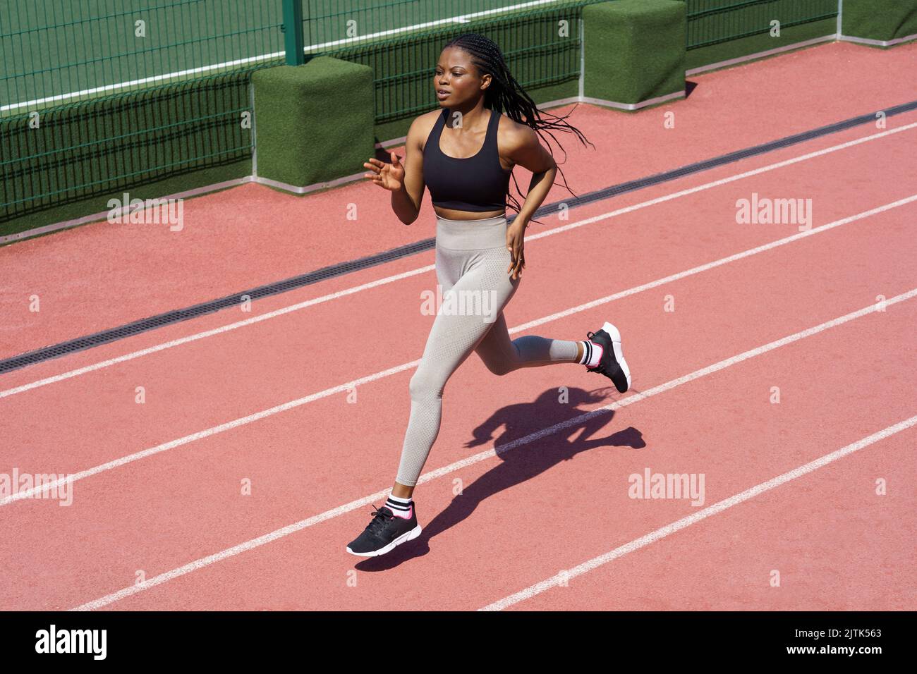 African woman athlete running on racetrack. Sportive black female training jog on stadium ...