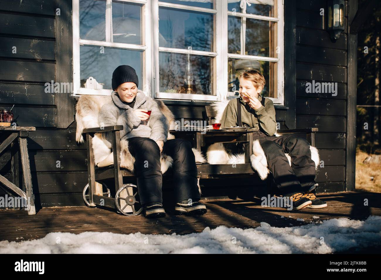 Full length of smiling friends sitting on chairs at porch during winter ...