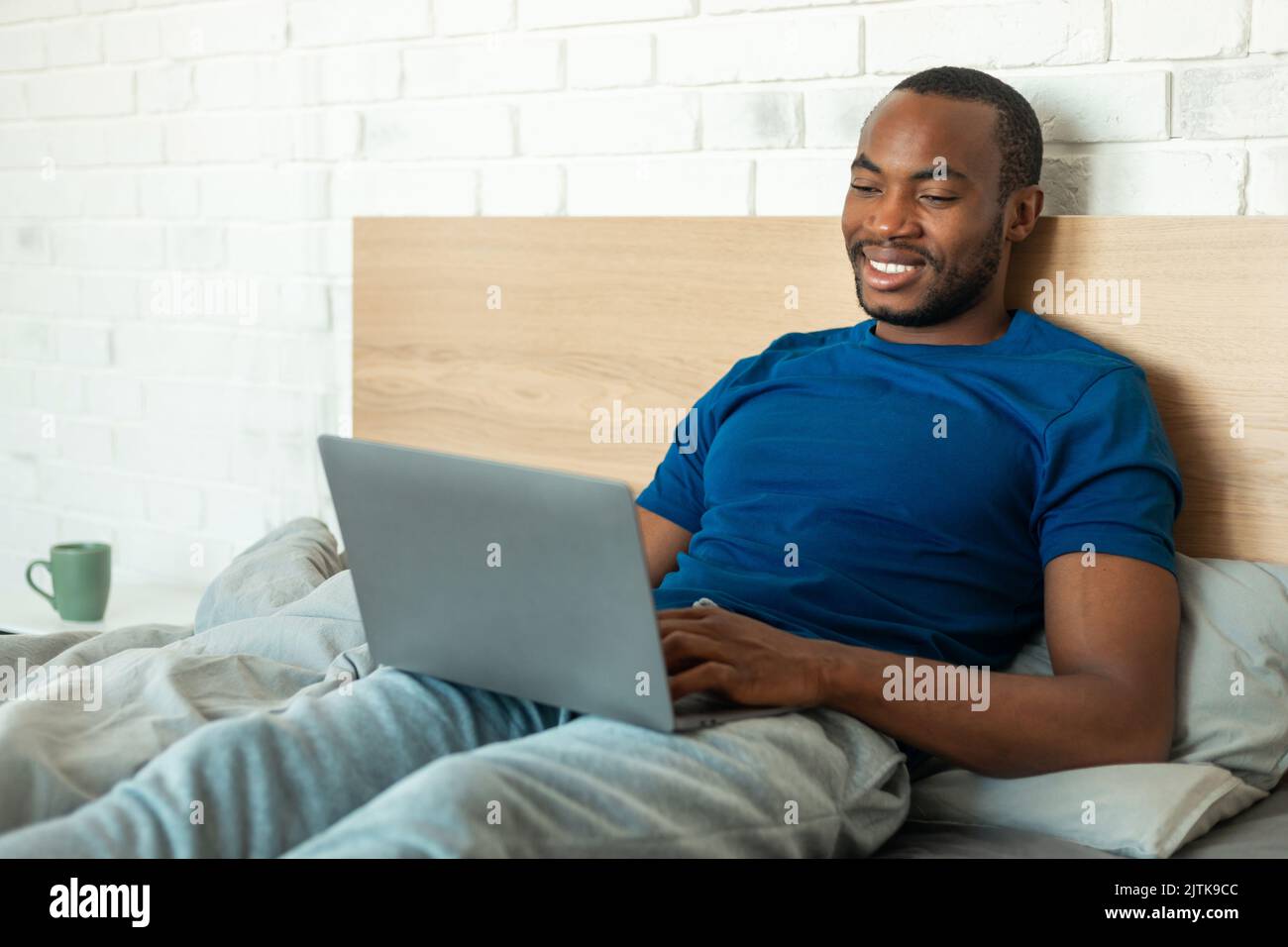 African American Guy Using Laptop Working Online Lying In Bedroom Stock ...