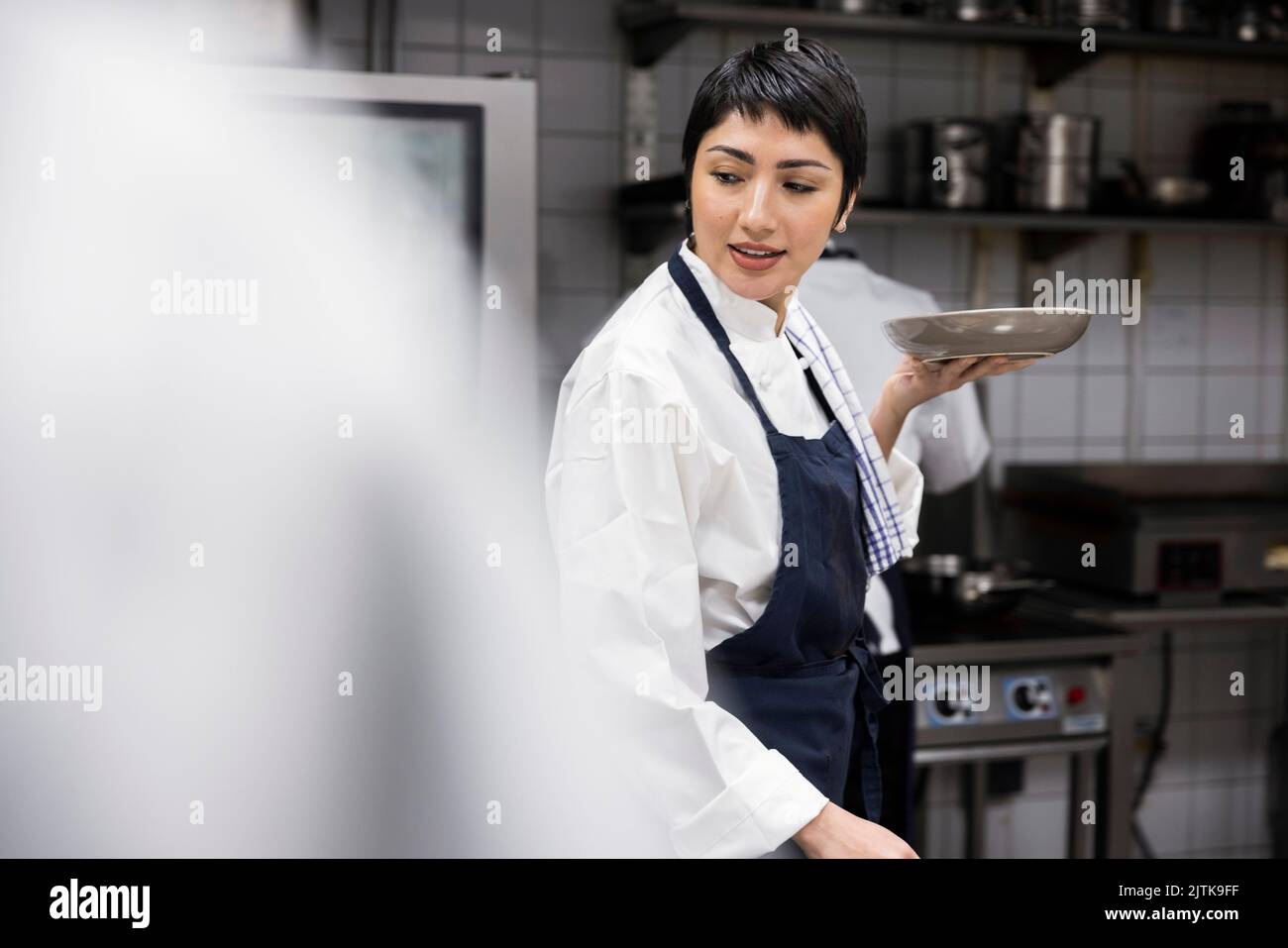 Chef with short hair carrying plate while working at restaurant kitchen ...