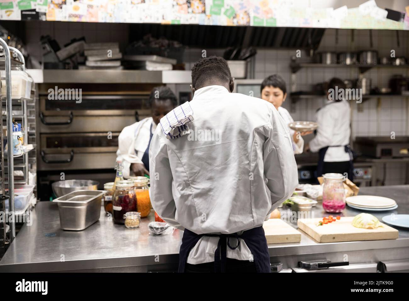 Rear view of chef working with colleagues in kitchen of restaurant ...