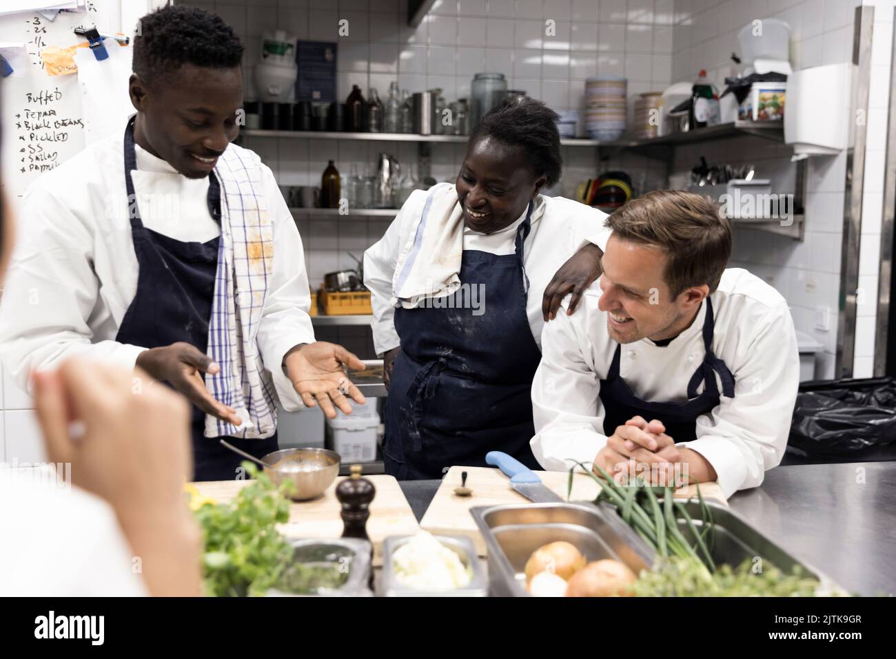 Chef explaining smiling multiracial colleagues at kitchen in restaurant ...