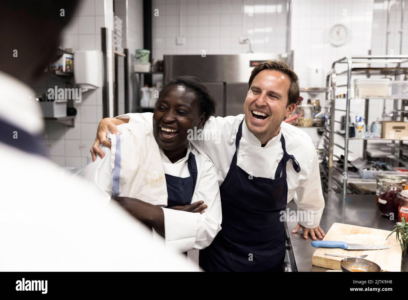 Happy chef with arm around female colleague in commercial kitchen Stock ...