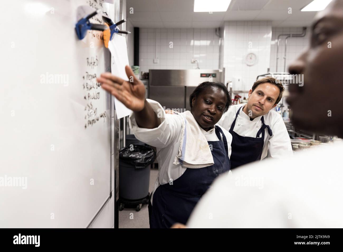 Female chef explaining colleagues over whiteboard in kitchen of ...