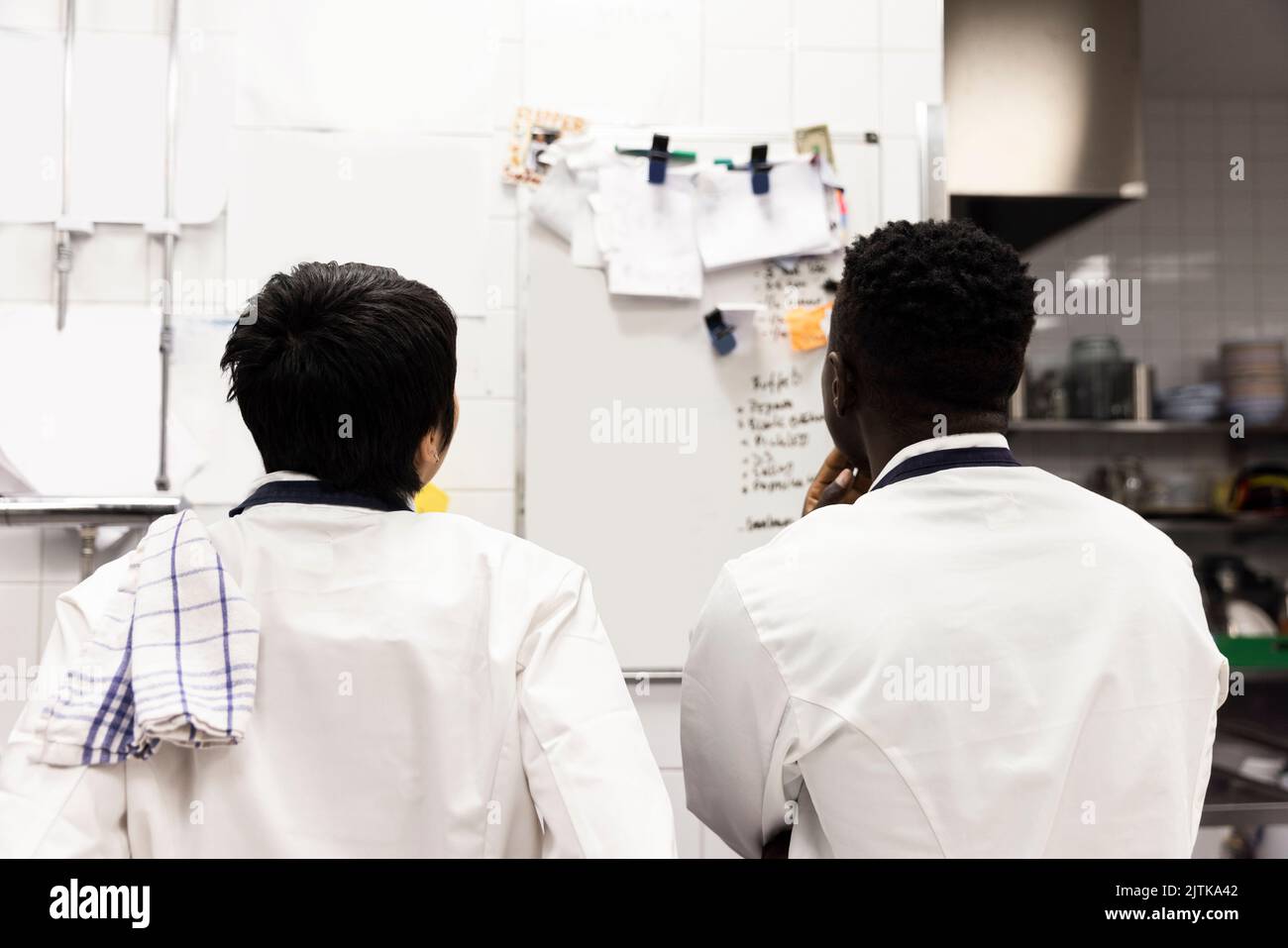 Rear view of multiracial chefs brainstorming over whiteboard in kitchen ...