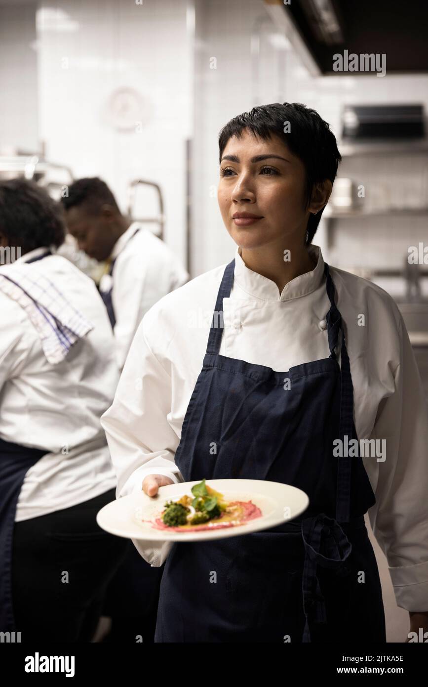 Female chef carrying plate of food while walking in kitchen of ...