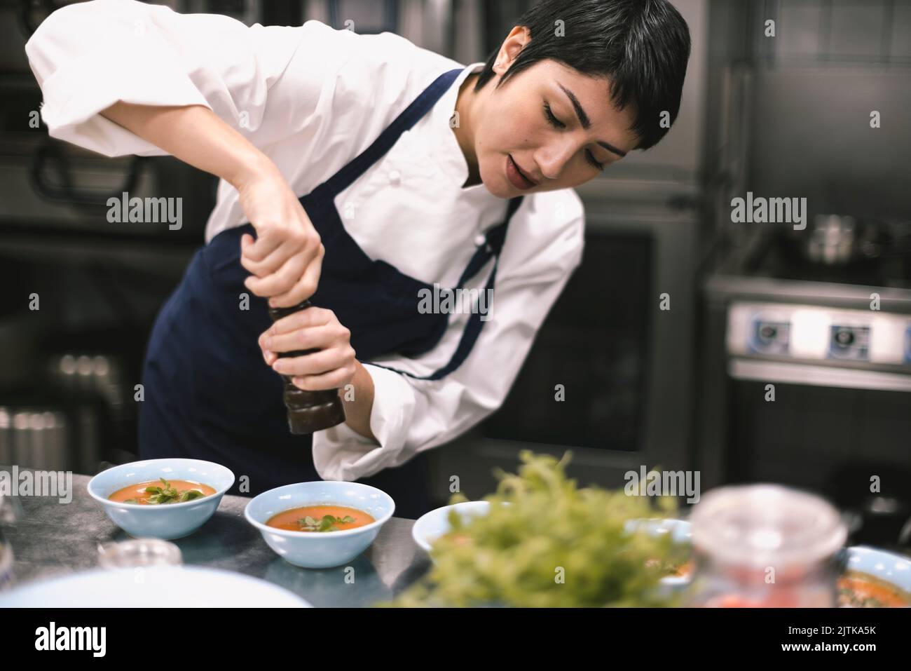 Female chef adding pepper in soup at kitchen counter in restaurant ...