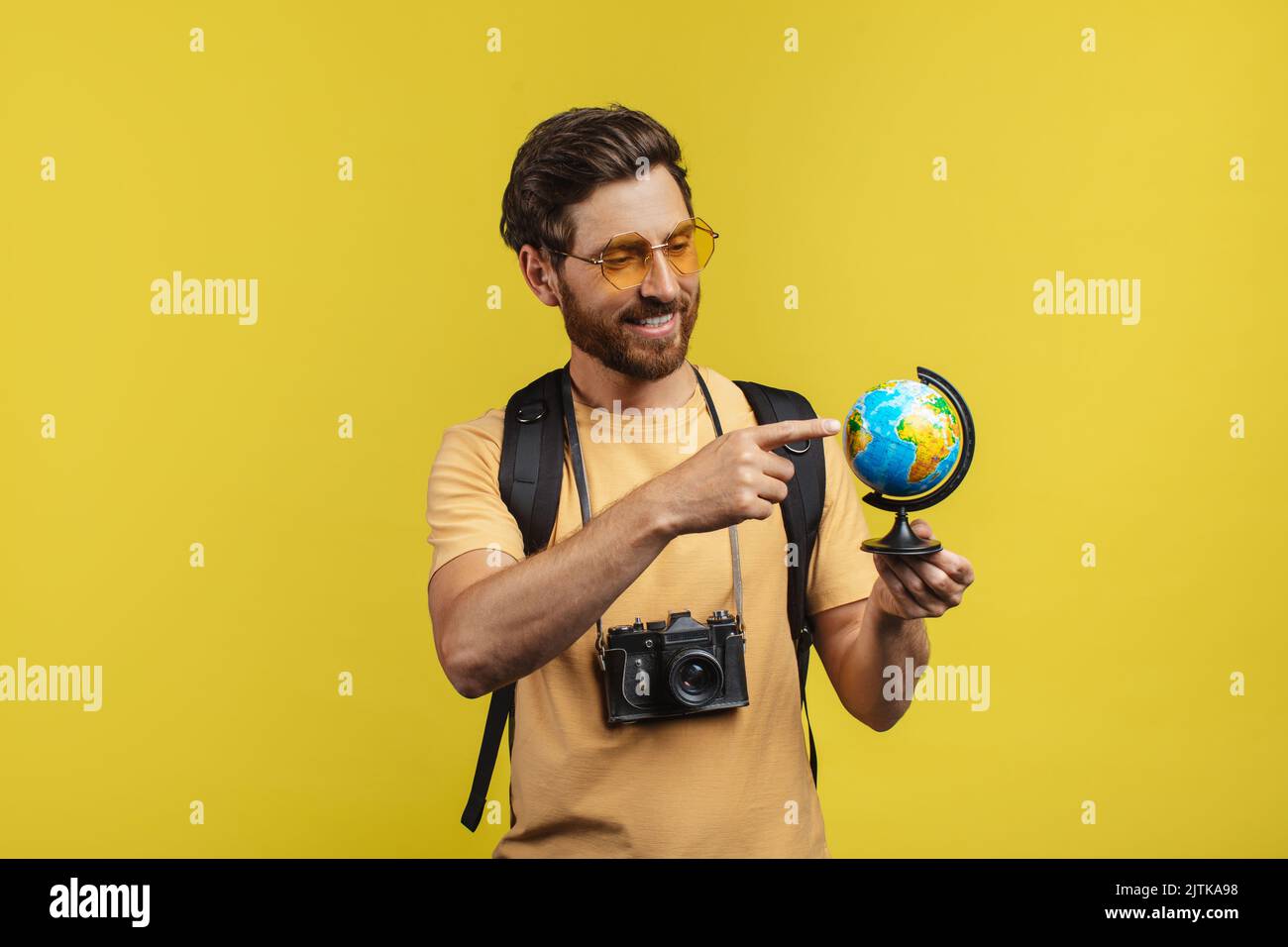 Happy male traveler holding world globe and pointing on it, wearing ...