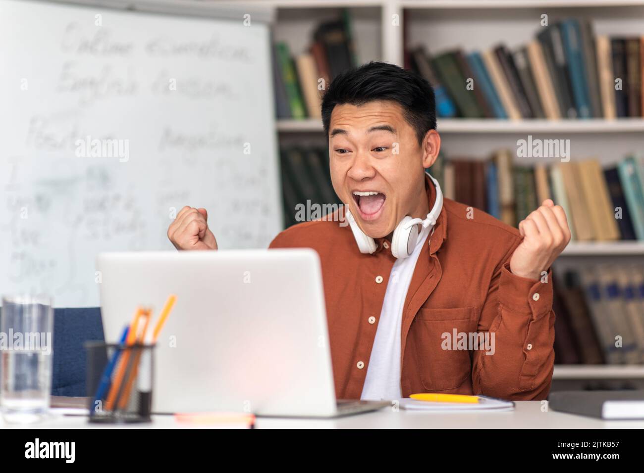 Emotional Asian Teacher Using Laptop Gesturing Yes Sitting In Classroom ...