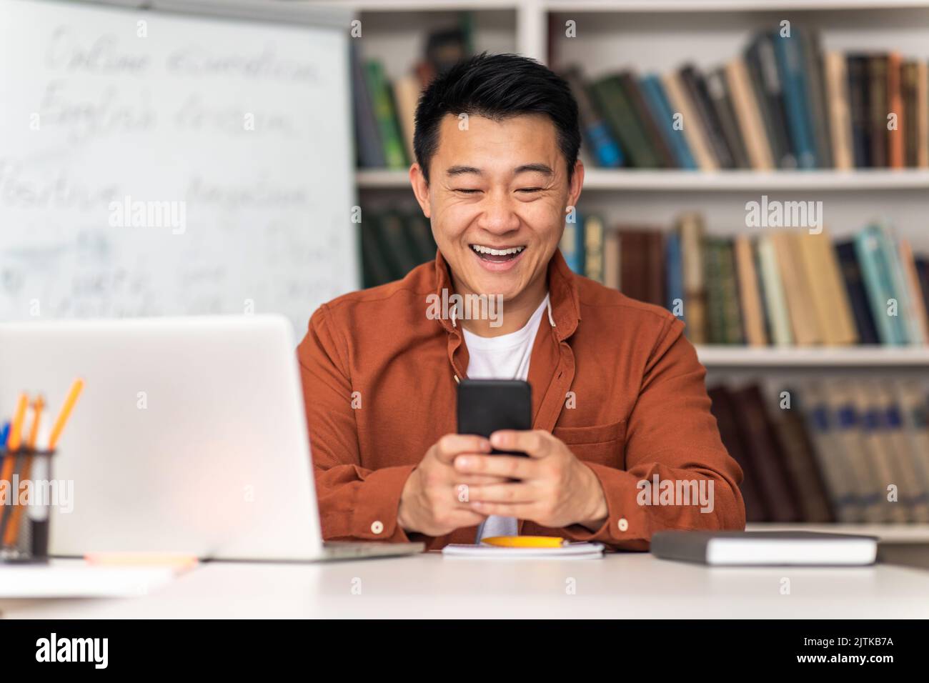Japanese Teacher Man Using Cellphone Sitting At Desk In Classroom Stock ...
