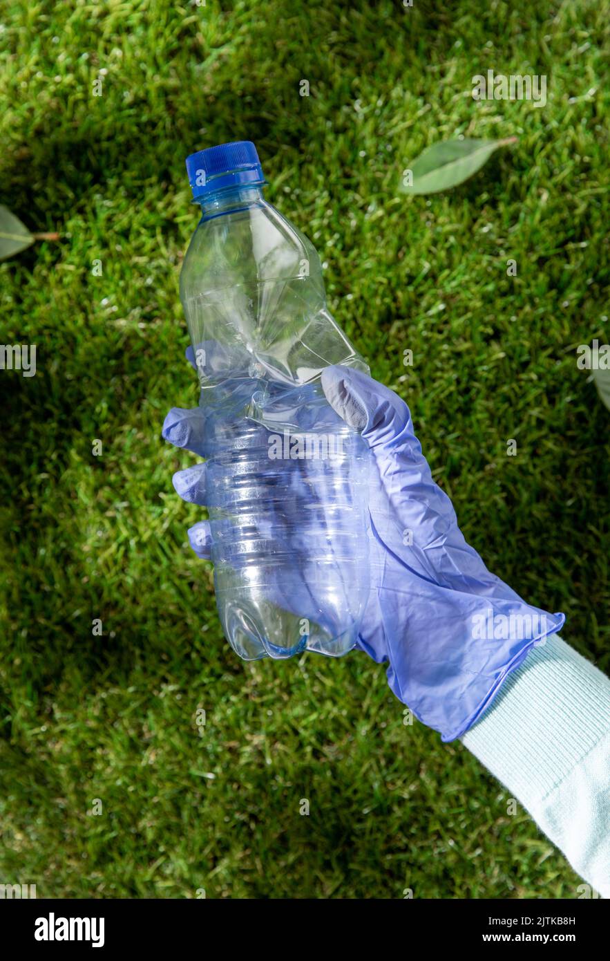 hand in glove picking plastic bottle from grass Stock Photo - Alamy