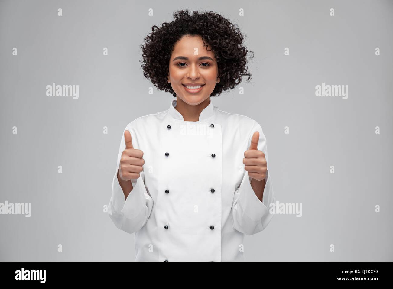 smiling female chef in jacket showing thumbs up Stock Photo - Alamy