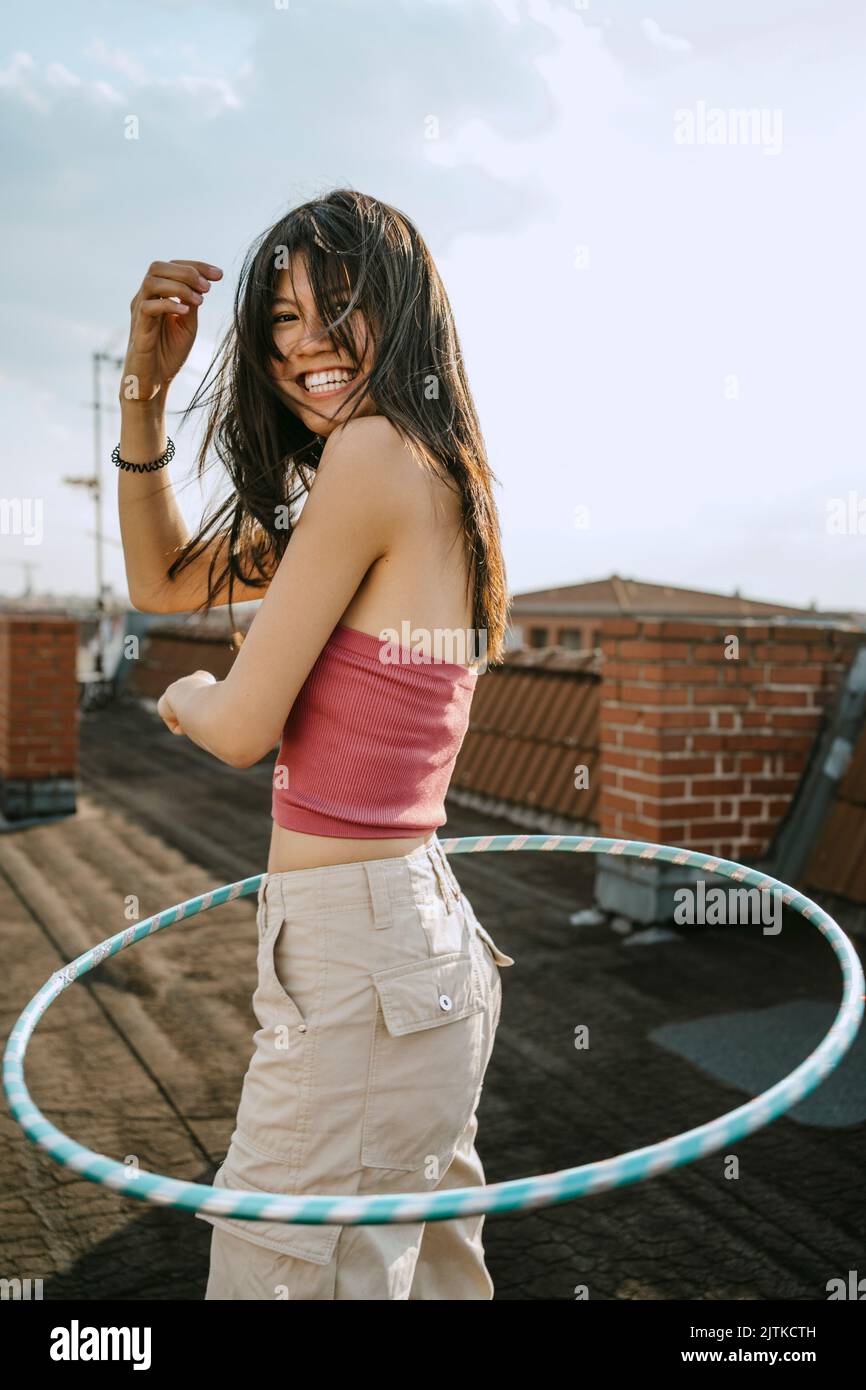Side view of cheerful woman spinning hoola hoop on rooftop Stock Photo ...
