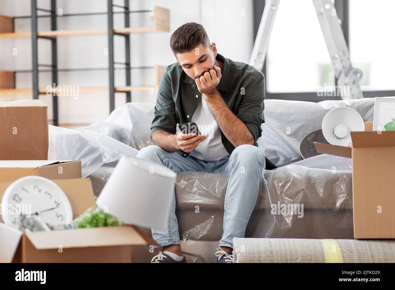 sad man with smartphone and boxes moving home Stock Photo - Alamy