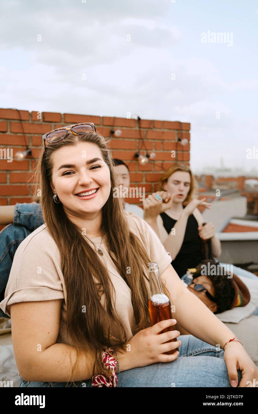 Portrait of smiling young woman holding beer bottle sitting in front of ... Portrait of smiling young woman holding beer bottle sitting in front of ...