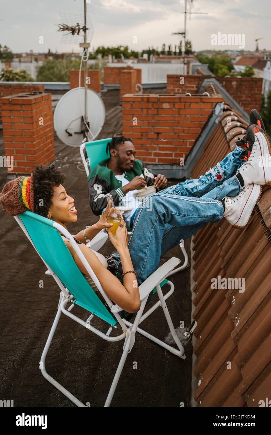 Full length of female and male friends sitting with feet up on chair at ...