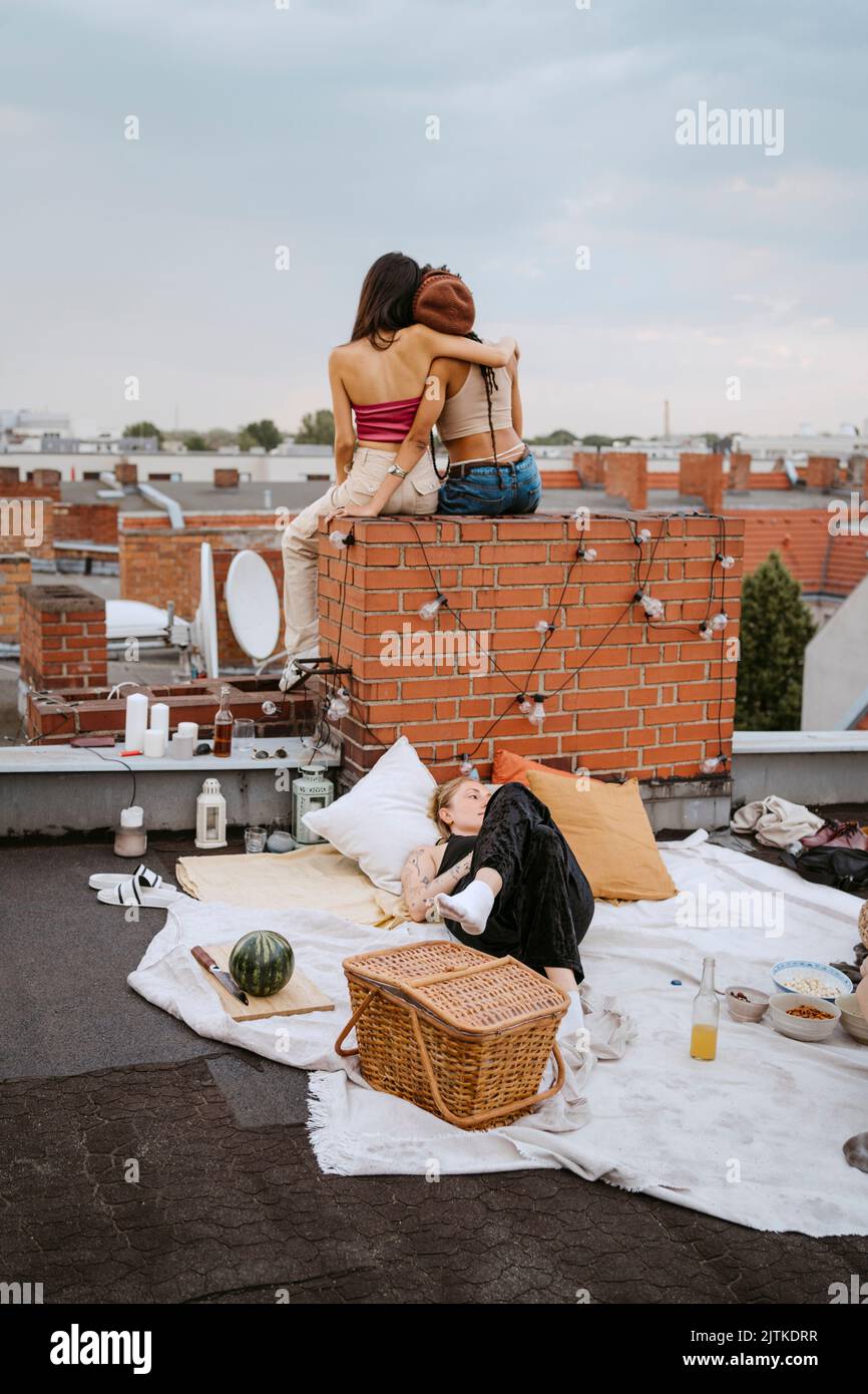 Woman lying on blanket with female friends sitting with arms around at ...