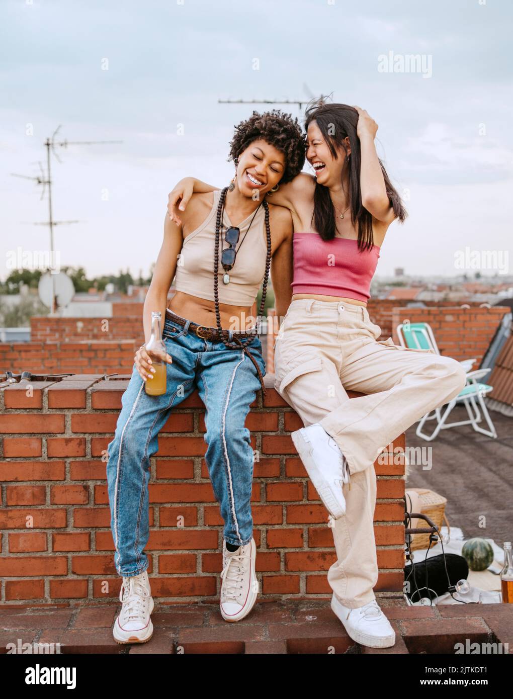 Full length of female friends laughing while sitting on rooftop Stock ...