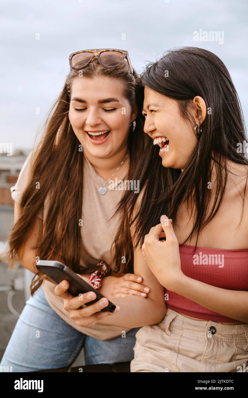 Young women laughing while sharing smart phone Stock Photo - Alamy