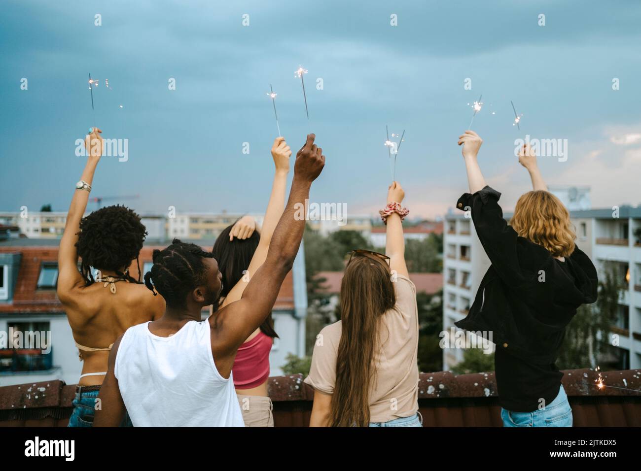 Rear view of multiracial friends with holding lit sparklers hands ...