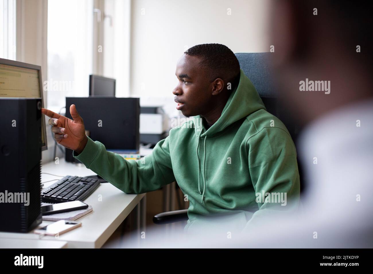Male trainee in hooded shirt pointing at desktop screen while ...