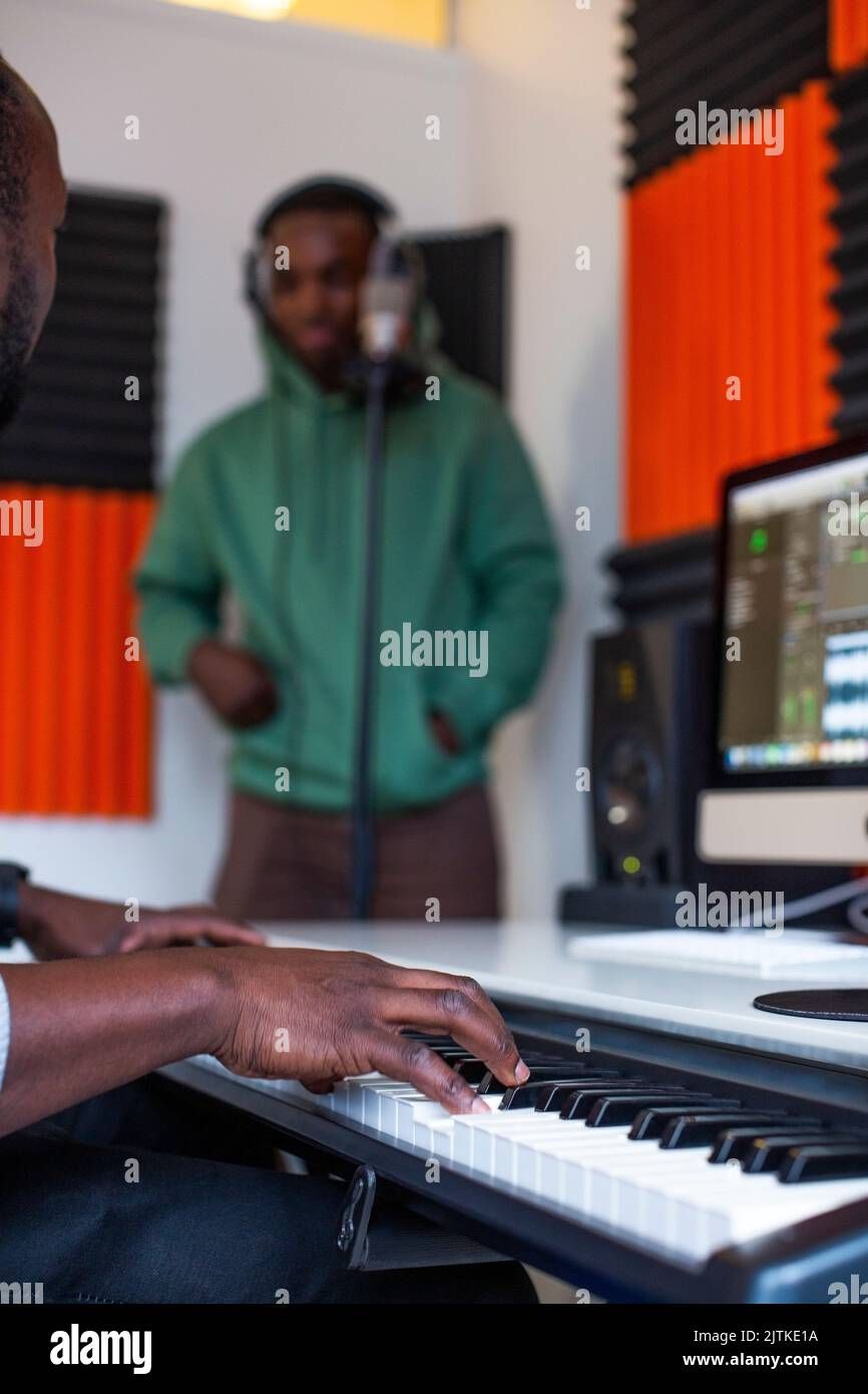Hands of sound engineer playing piano while rapper standing in ...