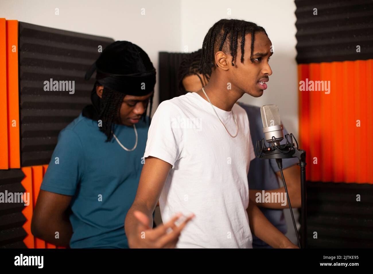 Teenage rapper with friends recording song on microphone in studio ...