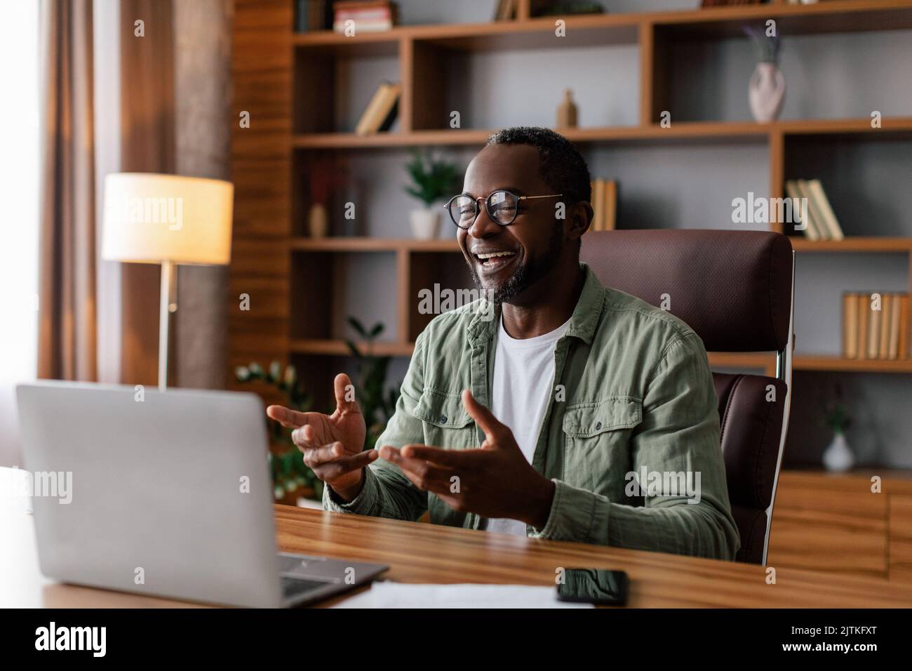 Laughing middle aged african american male in glasses works on laptop ...
