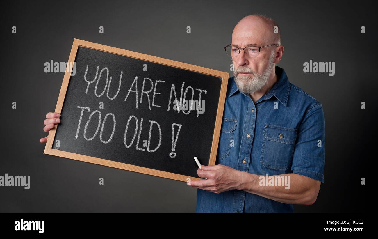 you are not too old blackboard sign held by a senior man in late 60s ...