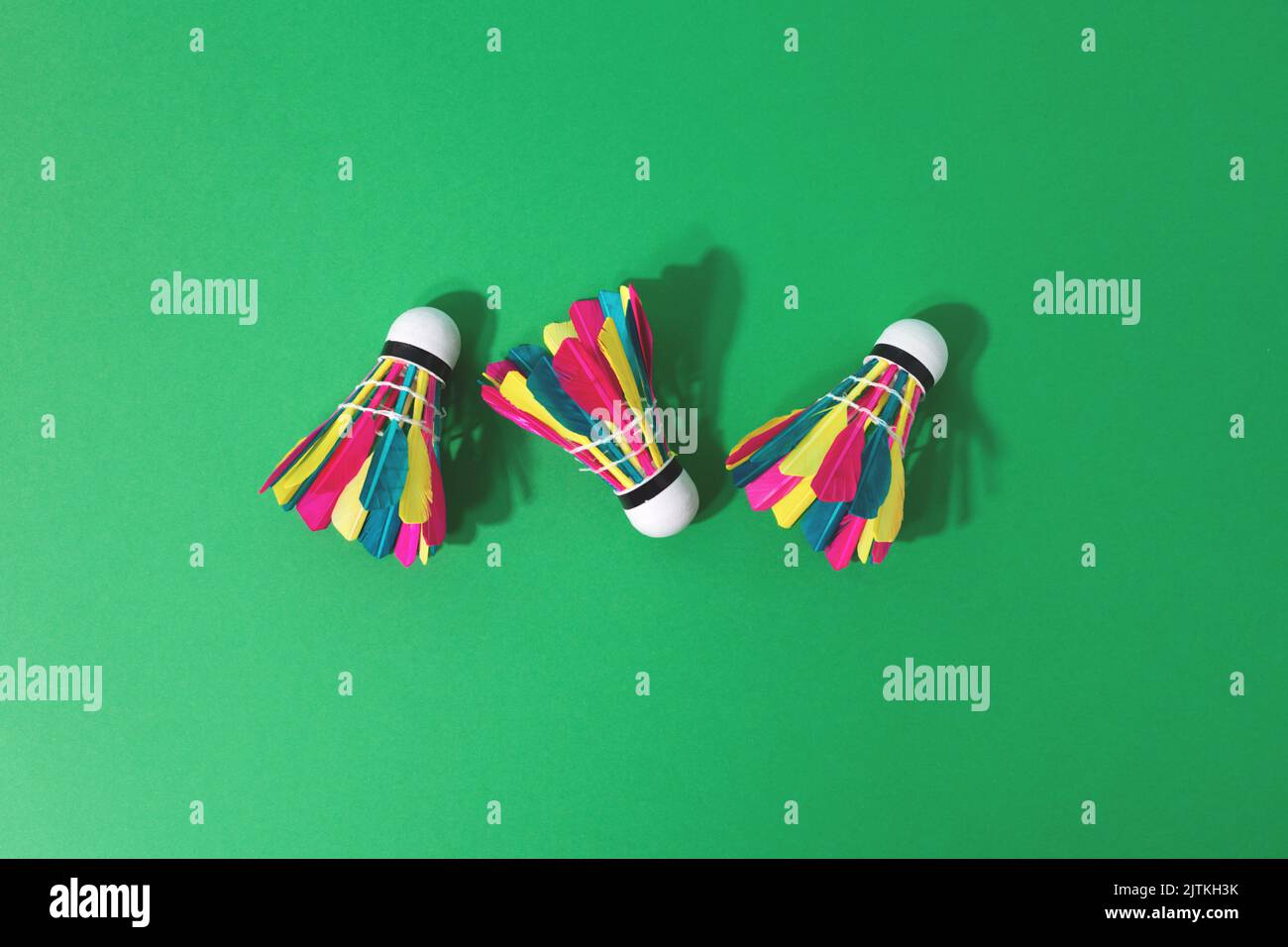 Top view of three feathered colourful shuttlecocks on green background ...
