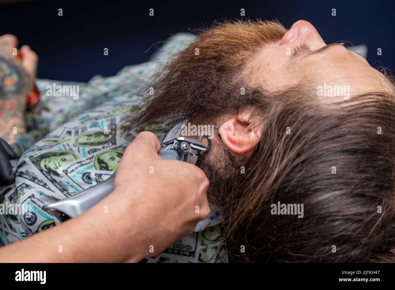 Barber using shaver to cut beard of a man Stock Photo - Alamy