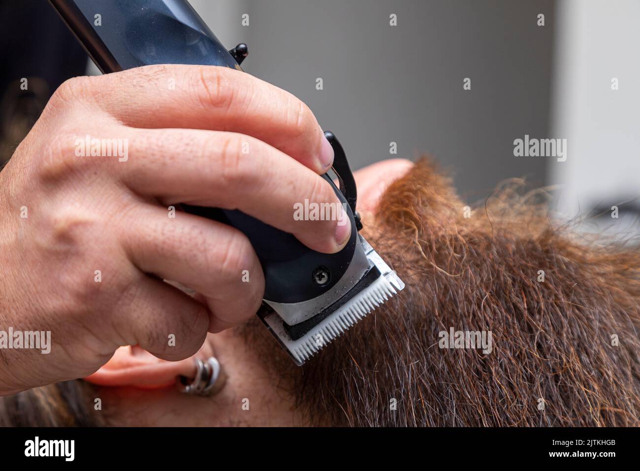 Barber using shaver to cut beard of a man Stock Photo - Alamy