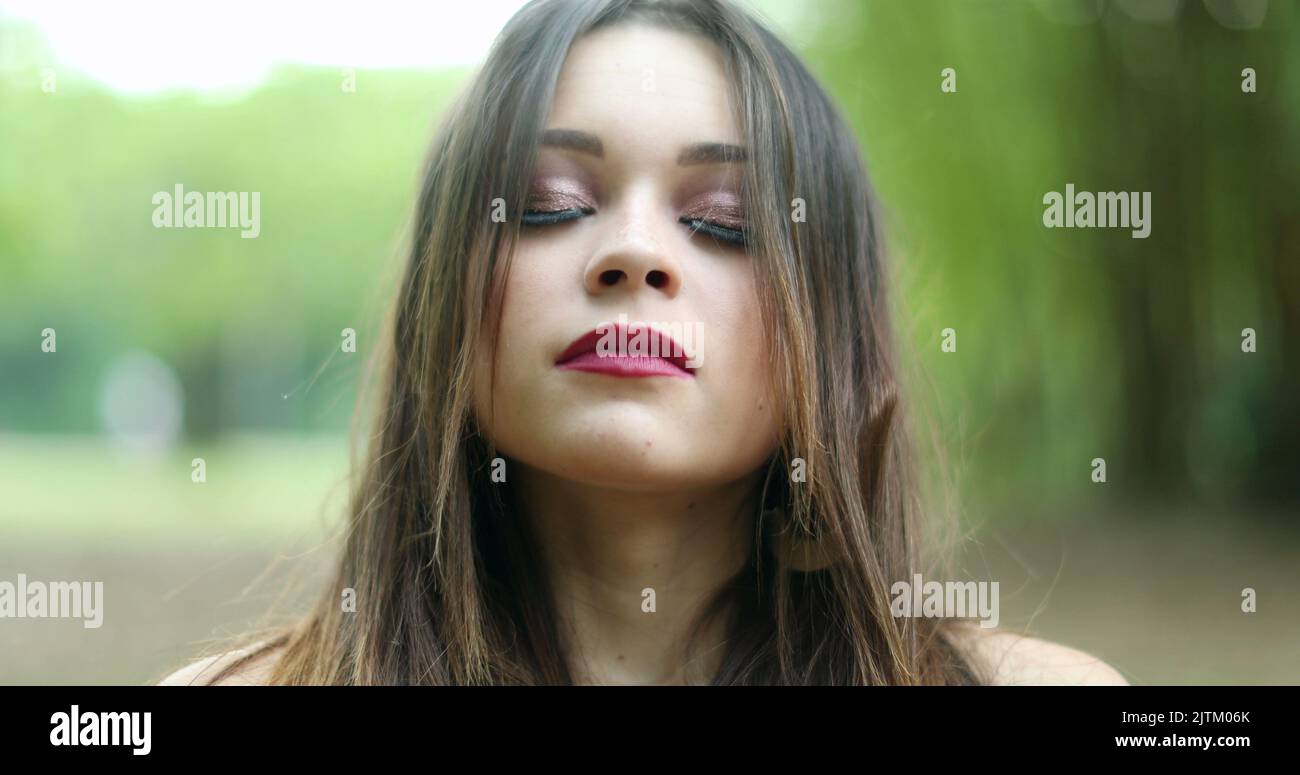 Young woman takes a deep breath outside, meditative pretty girl looking to camera feeling lungs ...