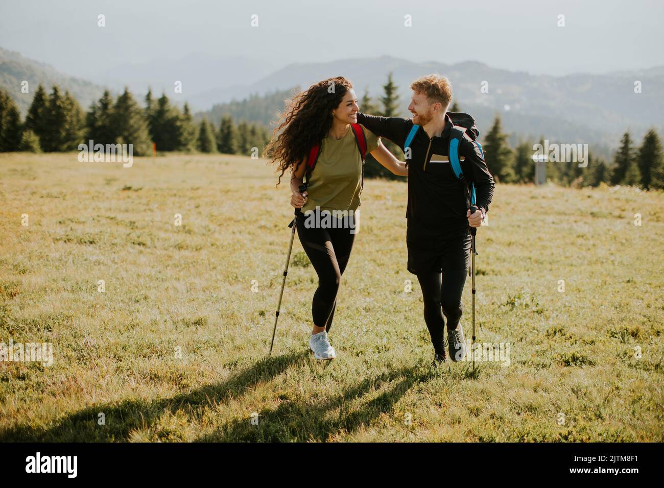 Smiling young couple walking with backpacks over green hills Stock ...