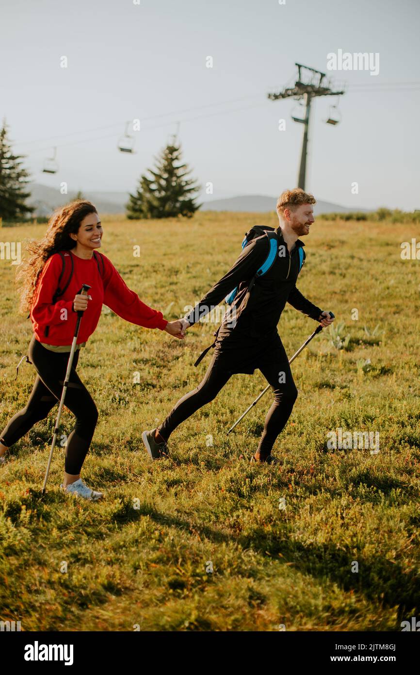Smiling young couple walking with backpacks over green hills by the ...